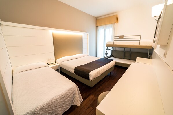 Quarto de hotel com duas camas, uma escrivaninha e uma cama beliche.