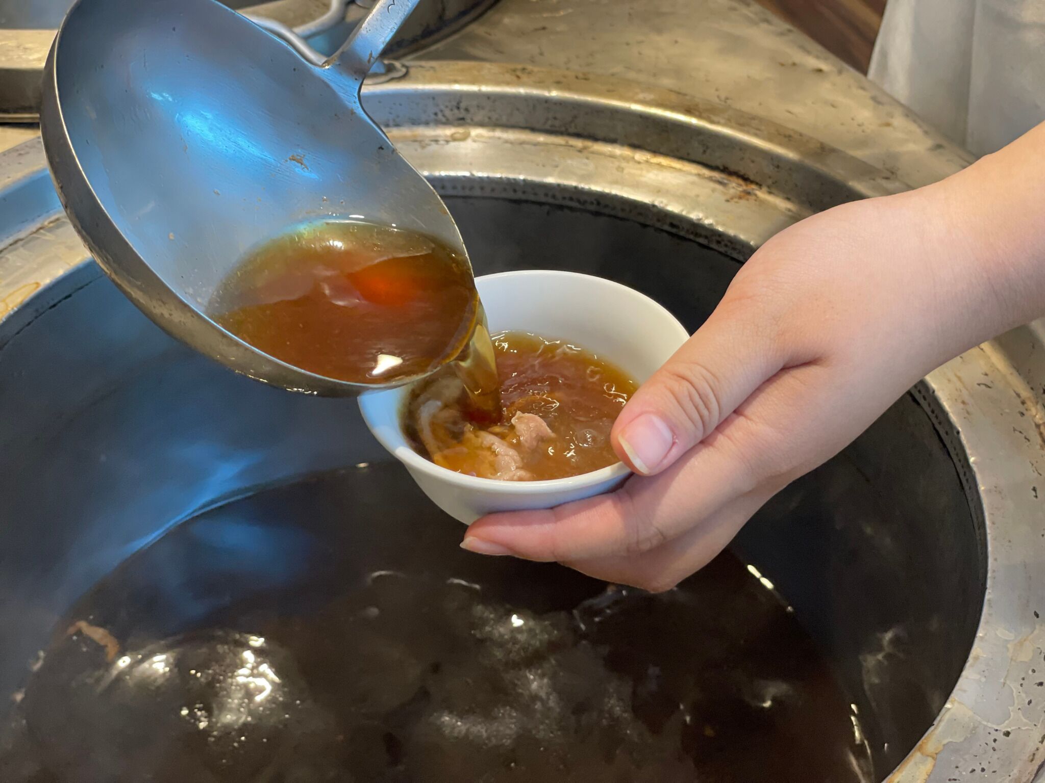 Alguém despejando líquido de uma panela para uma tigela.