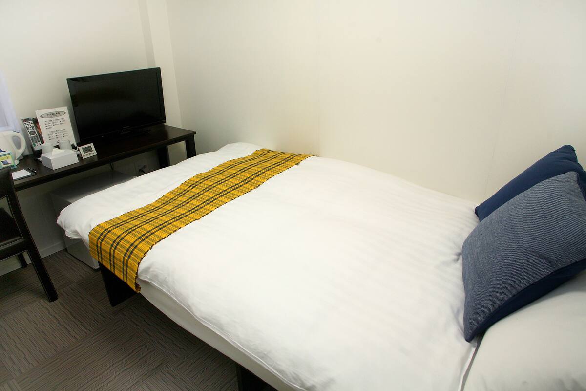 Quarto de hotel com cama, televisão sobre uma escrivaninha e cafeteira.