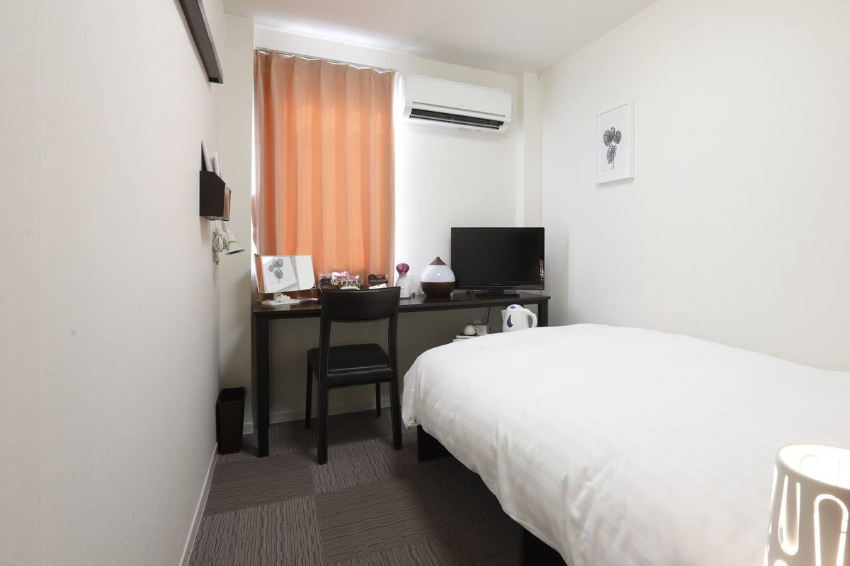 Quarto de hotel com cama, escrivaninha com computador, cadeira, televisão e ar condicionado.