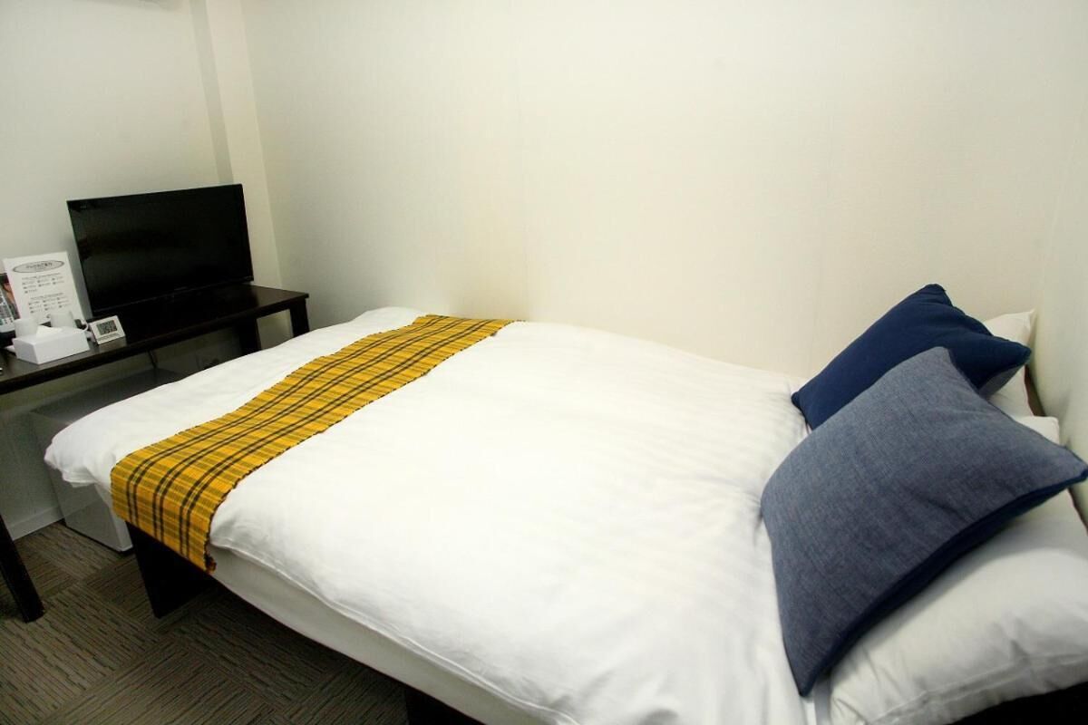 Quarto de hotel com uma cama, uma televisão sobre uma mesa e uma pequena mesa com telefone e um aviso.
