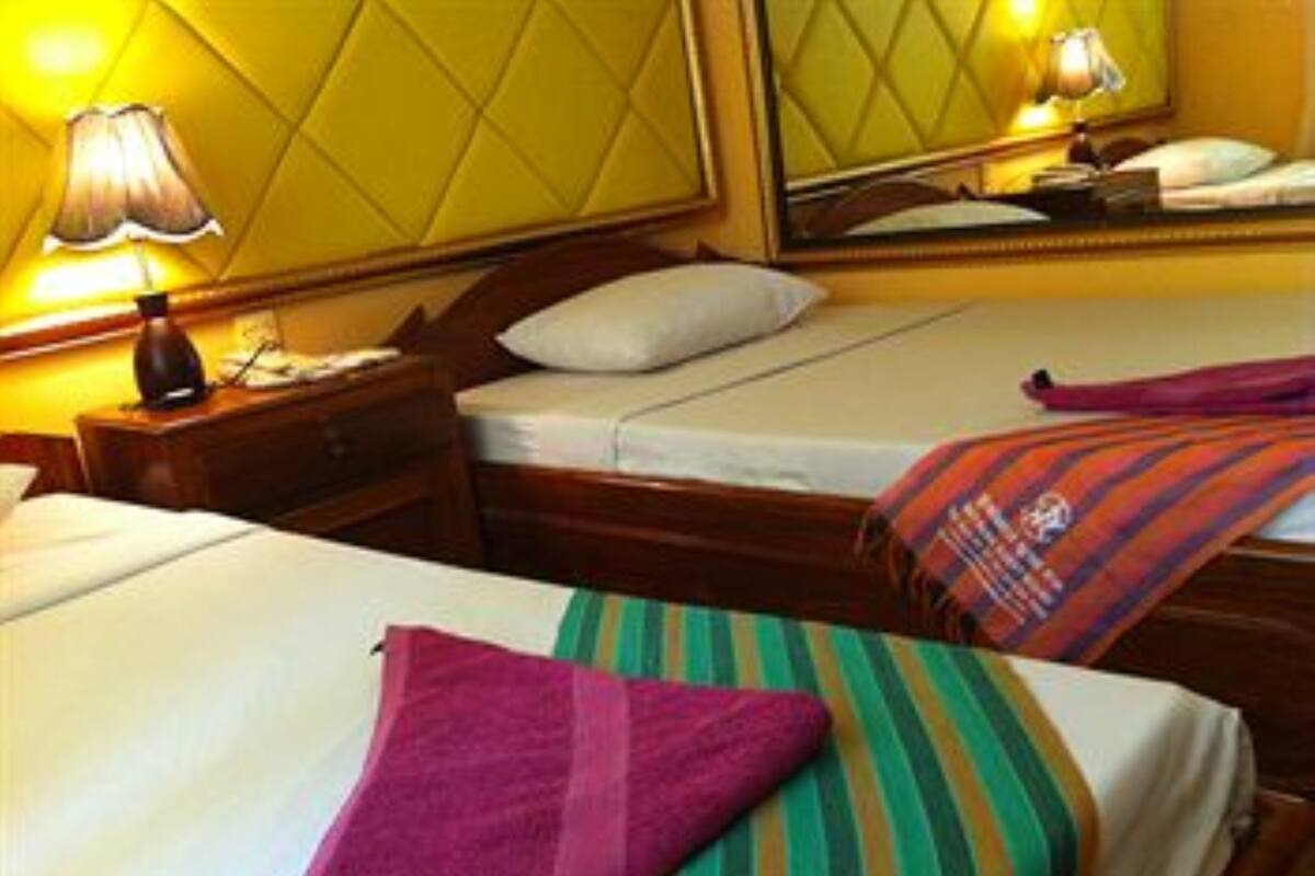 Quarto de hotel com duas camas, mesa de cabeceira com abajur, espelho e janela com cortinas amarelas.