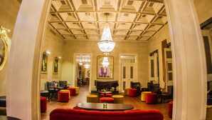 Um hall imponente com teto alto, colunas ricamente decoradas e um lustre central.