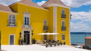 Um edifício amarelo com telhado em telhas, varanda e área de estar externa com guarda-sóis.