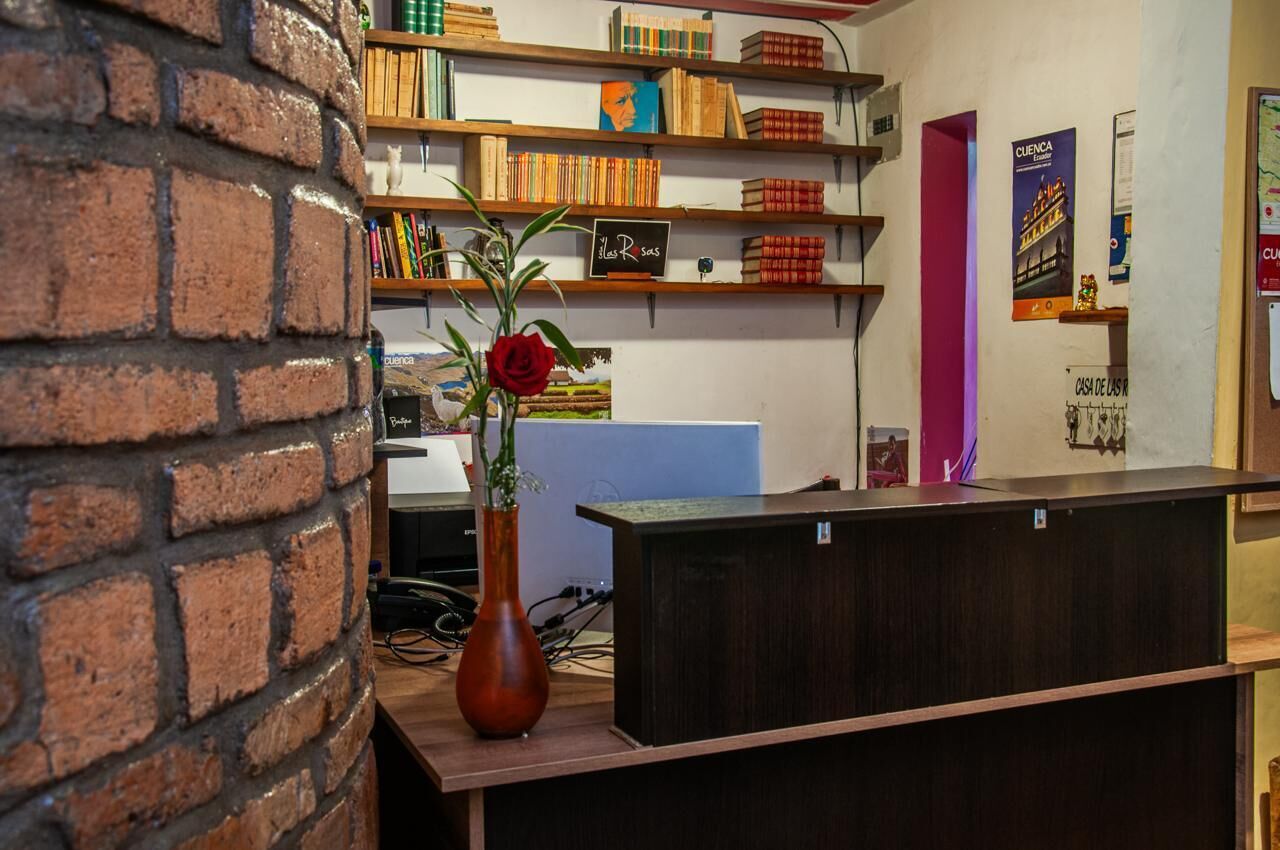 Uma mesa de recepção com um vaso de flores, uma estante de livros e uma parede de tijolos.