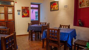 Restaurante com mesas e cadeiras de madeira, piso de azulejos e diversas decorações nas paredes, incluindo pinturas de frutas e uma ilustração de pássaro.