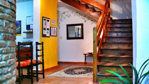 Uma escadaria que leva a um andar superior, uma cadeira de madeira, uma pequena mesa e uma parede com quadros emoldurados.