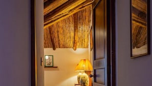 Um corredor estreito que leva a um quarto com teto de madeira, luminária na cabeceira e um quadro na parede.