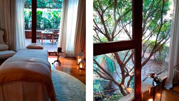 Quarto com cama, uma mesinha e vista para um jardim através de uma janela.