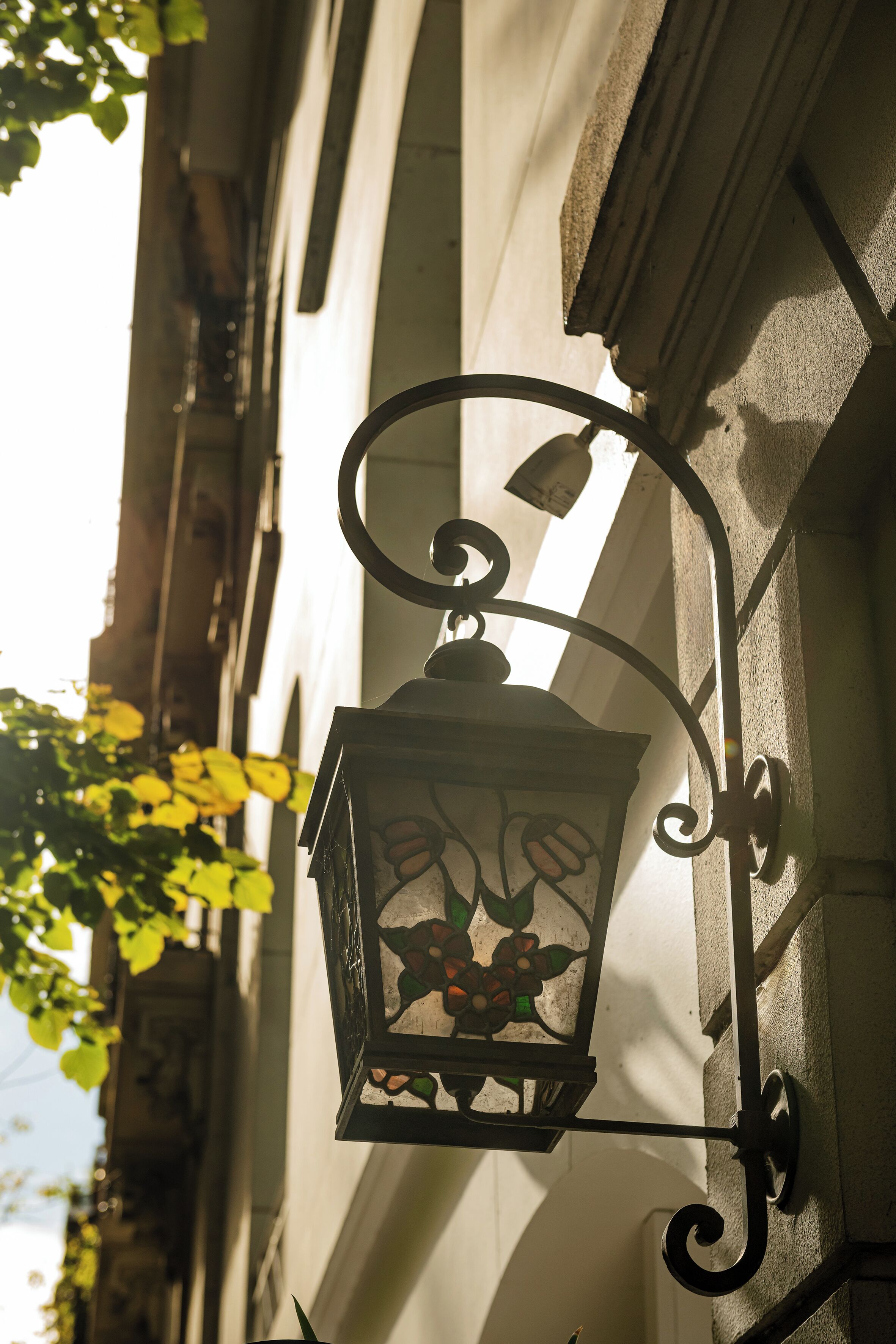 Luminária de metal com design floral pendurada na parede externa de um edifício.
