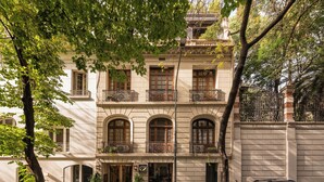 Um edifício de vários andares com estilo arquitetônico clássico, com janelas em arco e grades de ferro decorativas nas varandas.
