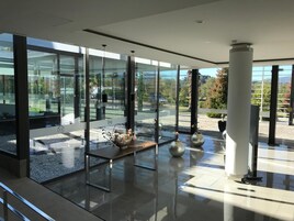 Um interior moderno com grandes janelas de vidro, uma mesa de madeira central com objetos decorativos e um elegante pilar branco.