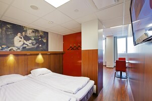 Quarto de hotel com duas camas, um quadro na parede, parede vermelha, uma televisão e uma cadeira.