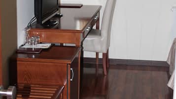 Quarto compacto com escrivaninha de madeira, televisão, cadeira e janela com cortinas.