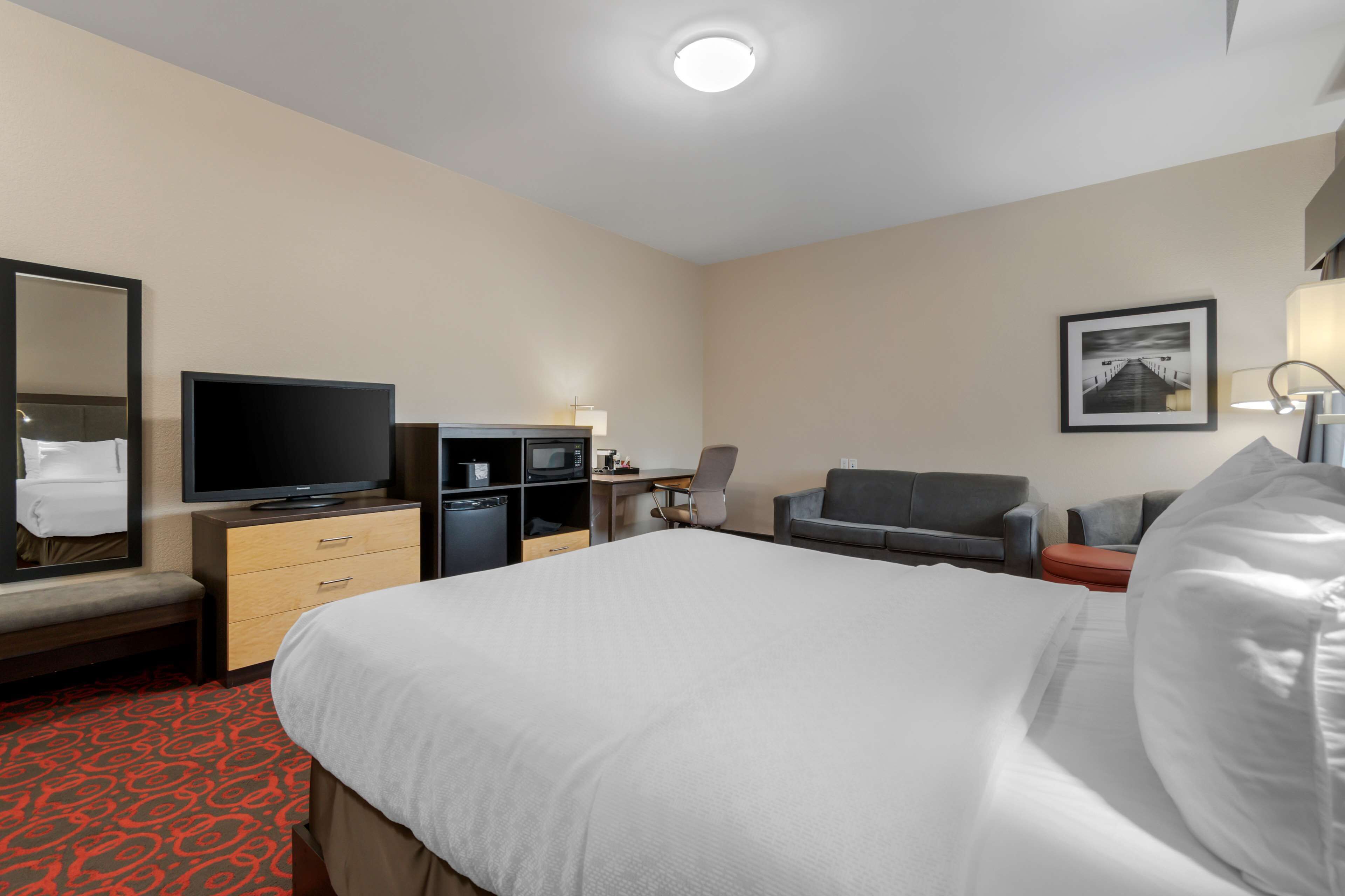 Quarto de hotel com cama, televisão, escrivaninha com cadeira, sofá e mesa de apoio com abajur.