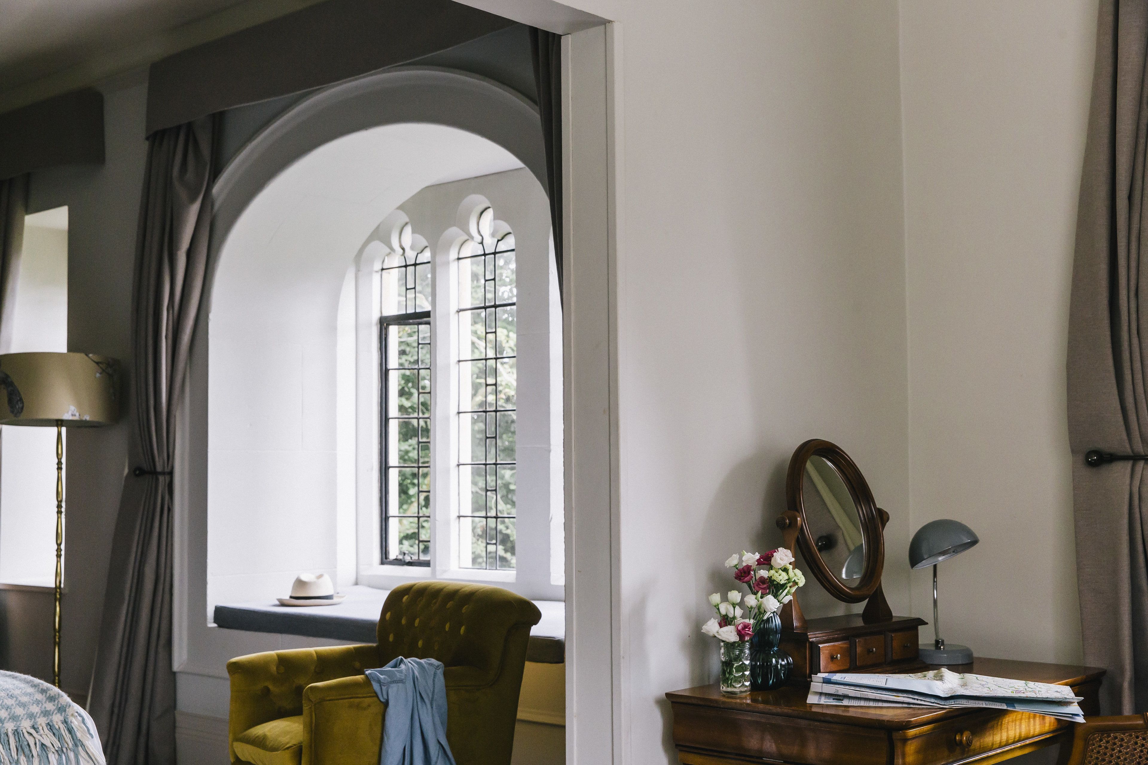 Quarto com uma grande janela em arco, cômoda de madeira, espelho e poltrona amarela.