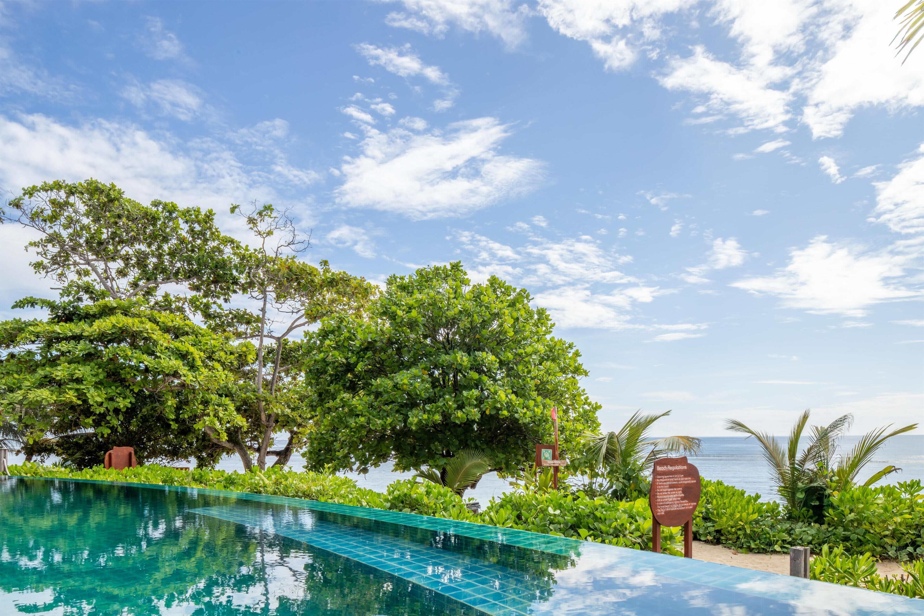 Piscina com vista clara do oceano, rodeada por vegetação exuberante e céu limpo.