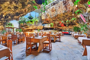 Um restaurante com mesas e cadeiras dispostas em fileiras, piso de pedra e plantas penduradas.