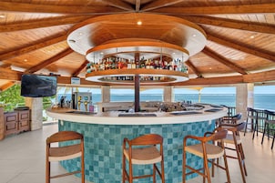 Um bar com design circular, diversas garrafas de bebidas, uma televisão e vista para o oceano.