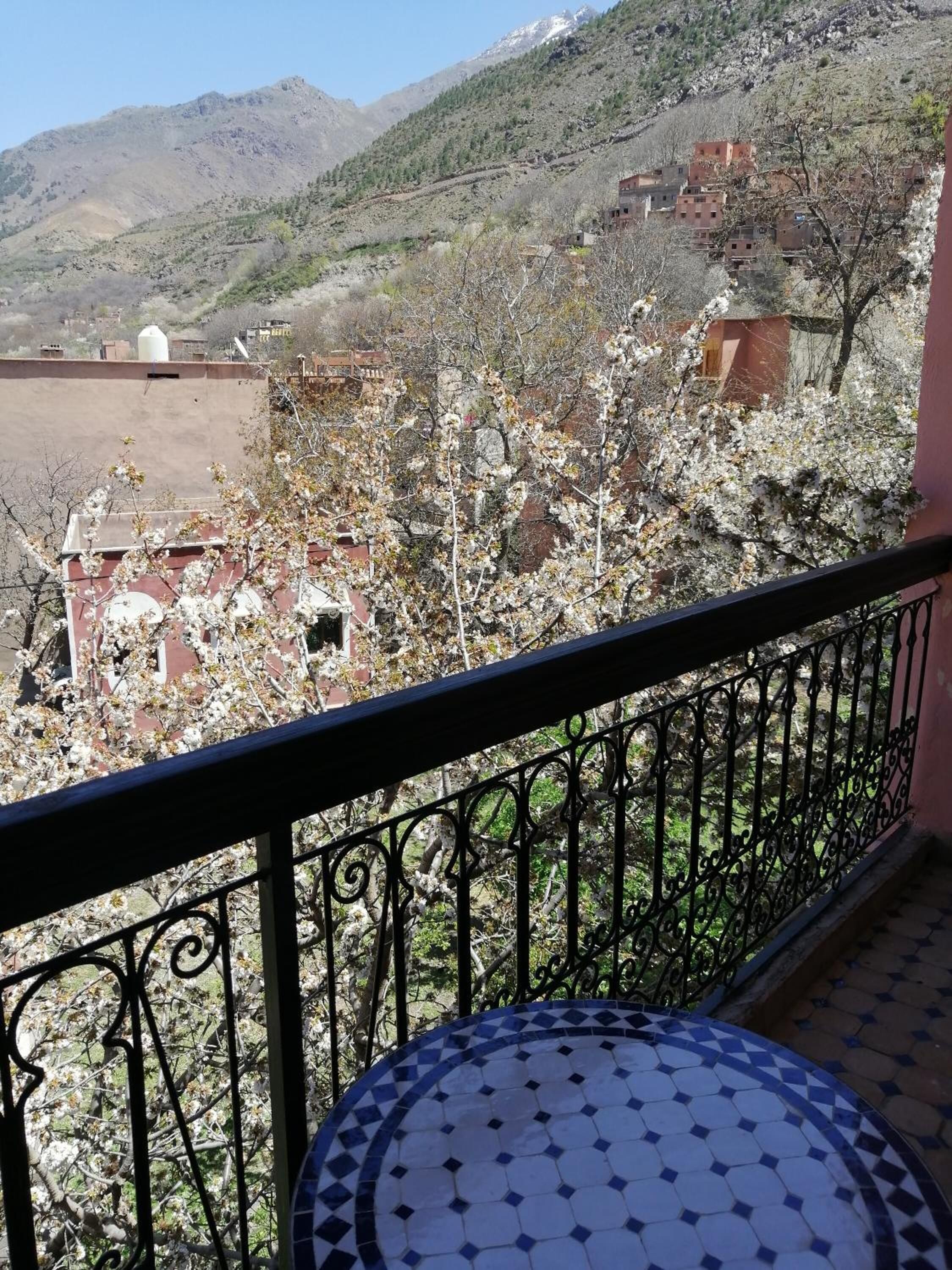 Varanda com piso de azulejos e guarda-corpo de metal, com vista para uma região montanhosa com vegetação escassa e edifícios.