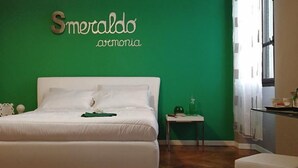 Quarto com parede verde, cama branca e uma pequena mesa de cabeceira com uma garrafa verde.