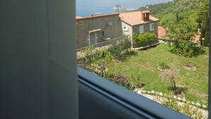 Vista da janela com uma casa e telhado vermelho, rodeada por vegetação e um corpo d'água ao longe.