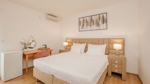 Quarto de hotel com cama, mesas de cabeceira, escrivaninha e um pequeno frigorífico.