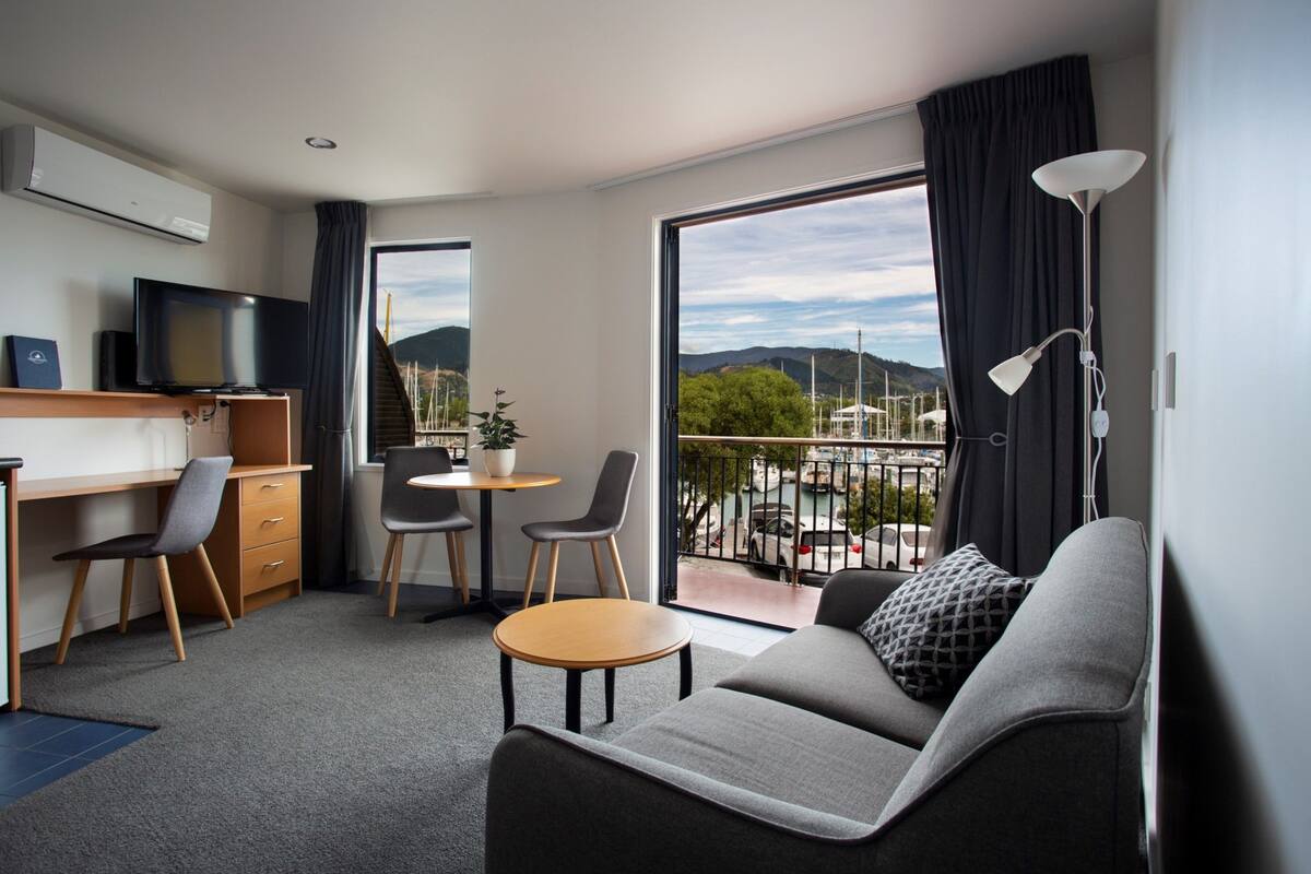 Quarto de hotel moderno com varanda, escrivaninha, sofá e televisão.
