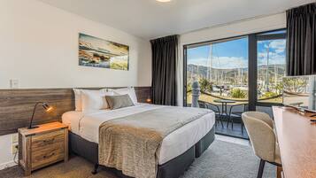Quarto de hotel com cama, mesa de cabeceira, escrivaninha e vista para um porto através de uma grande janela.