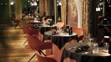 Restaurante com mesas redondas, cadeiras laranja e toalhas de mesa pretas.