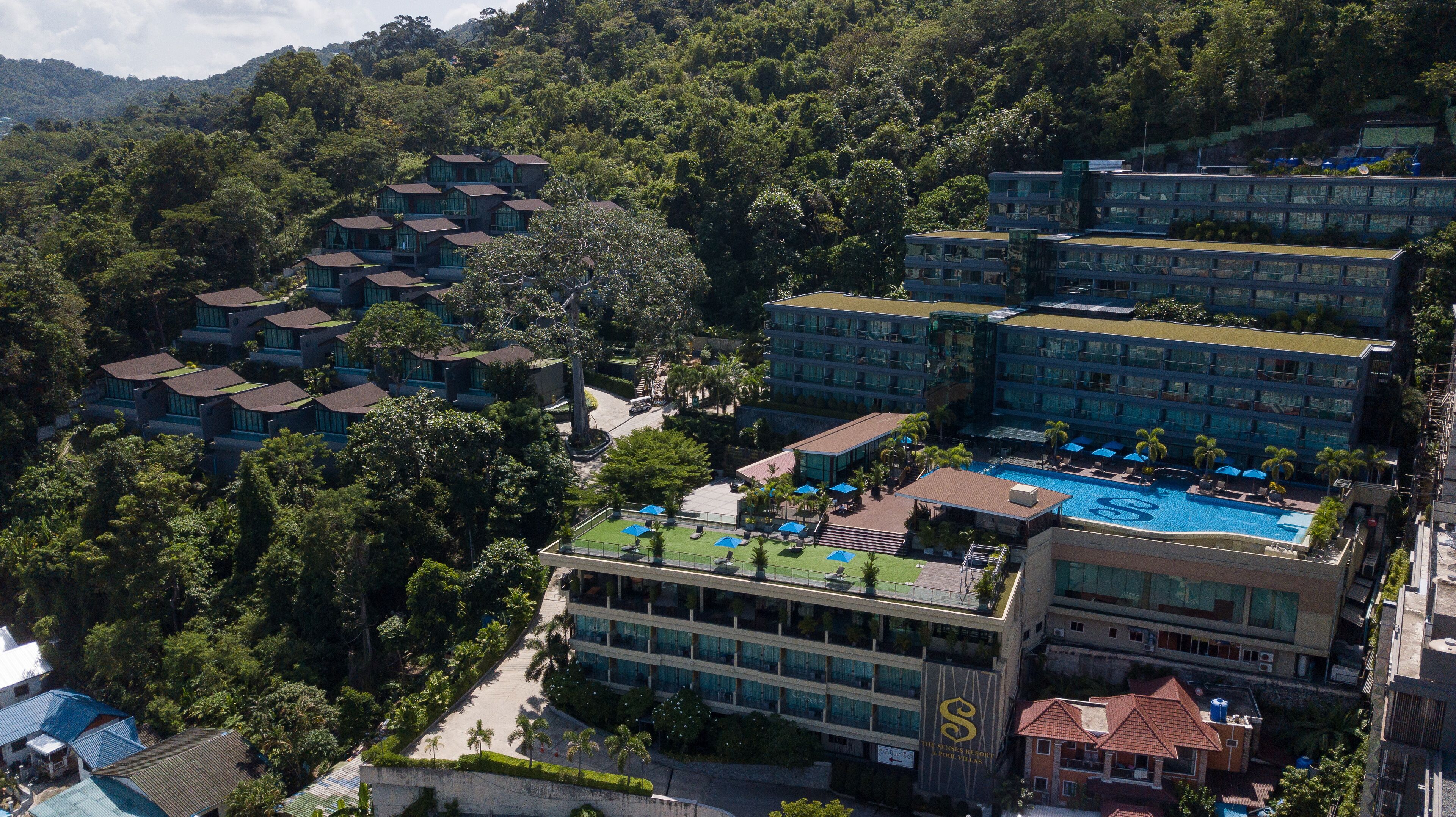 Um resort com vários edifícios, piscina e vegetação exuberante ao redor.