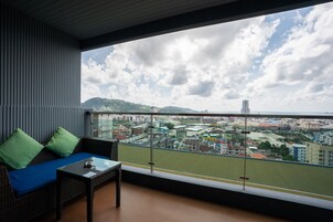 Varanda com sofá de vime e mesa de vidro, com vista para um horizonte urbano com edifícios e vegetação.