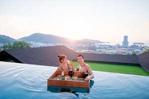 Um casal relaxando em uma piscina no terraço, com vista para a cidade.