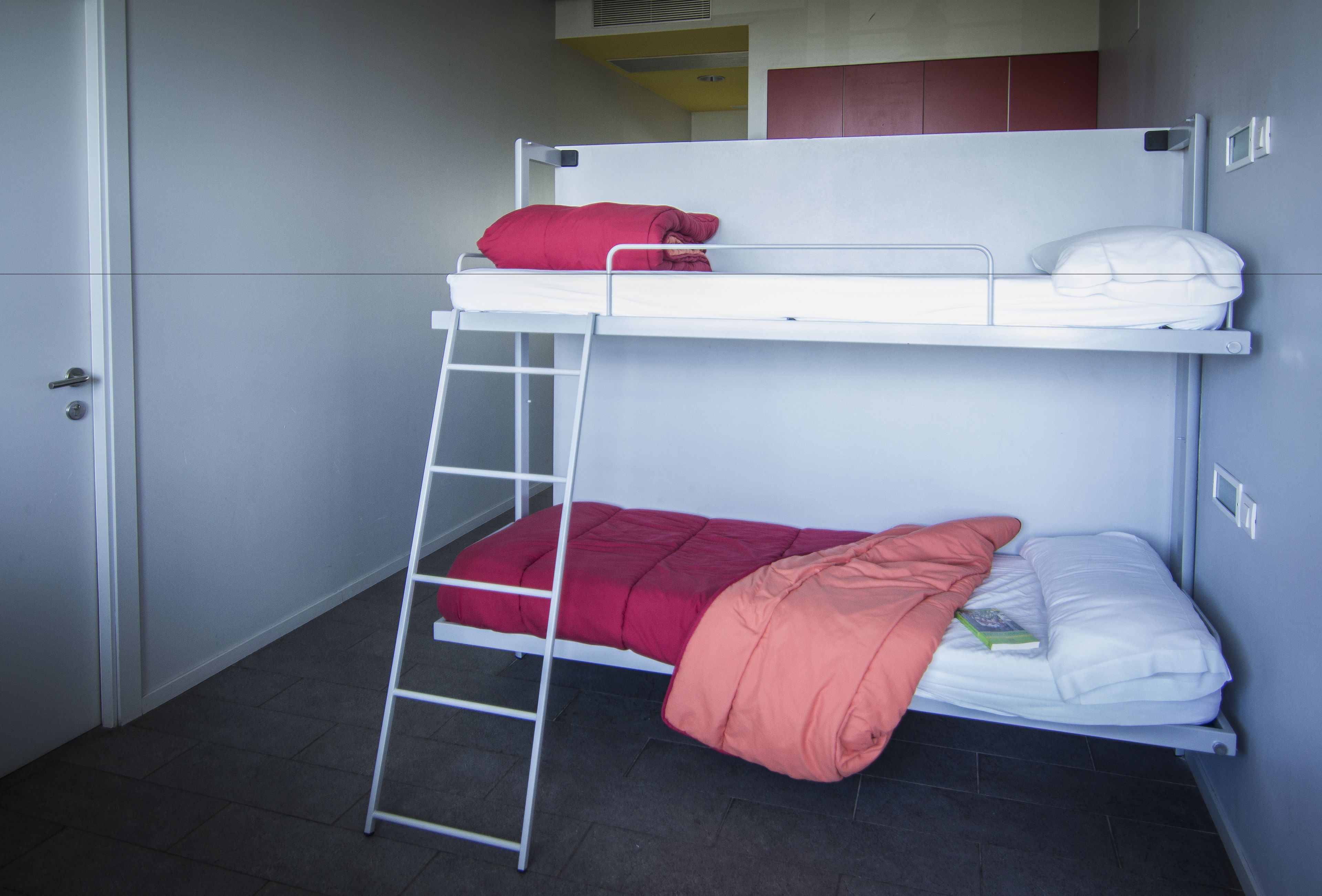 Quarto com beliche, uma escada, um cobertor vermelho e um colchão branco.
