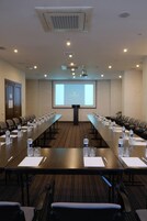 Uma sala de conferência com uma mesa comprida, cadeiras, garrafas de água e uma tela de projetor.