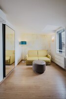 Uma sala de estar moderna com um sofá amarelo, um banquinho redondo, um abajur e um espelho grande.