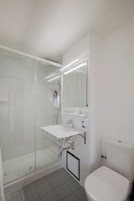 Casa de banho moderna com cabine de duche em vidro, lavatório branco com espelho em cima e sanita.
