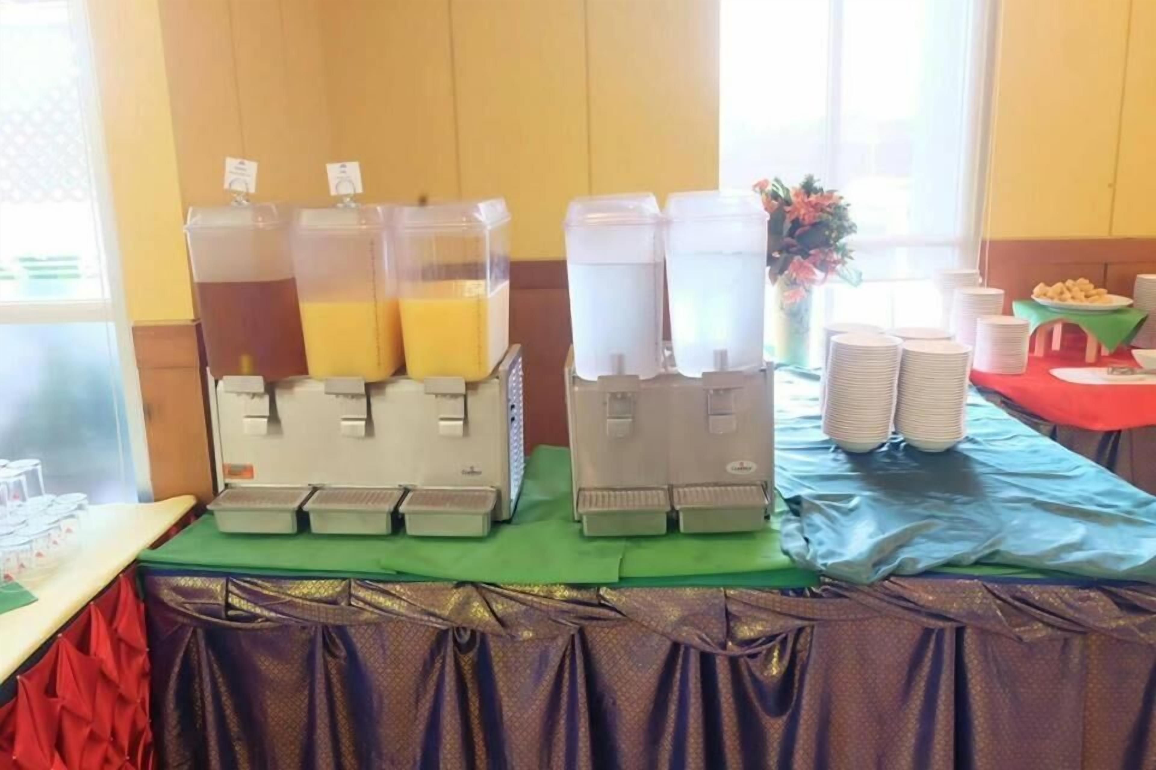 Disposição de buffet com vários distribuidores de bebidas e pilhas de pratos sobre uma mesa.