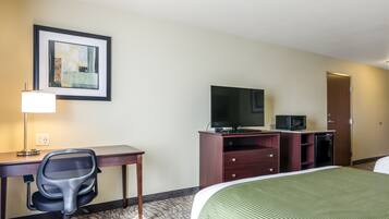 Quarto de hotel com cama, escrivaninha, cadeira, televisão, micro-ondas e porta.