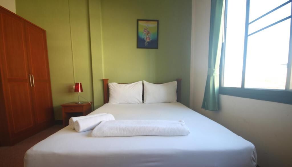 Quarto de hotel com uma cama, mesa de cabeceira, abajur e guarda-roupa.