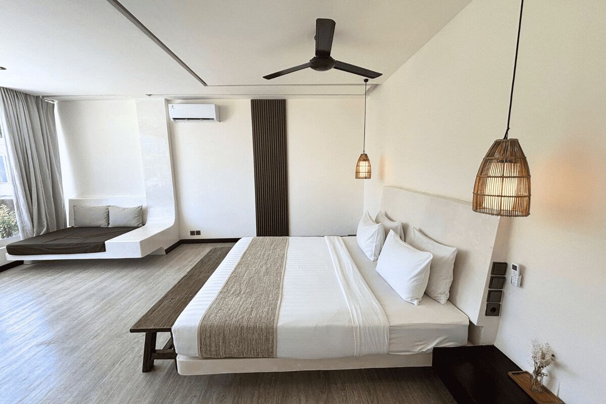 Quarto de hotel moderno com cama, um banco, ventilador de teto e janela com cortinas.