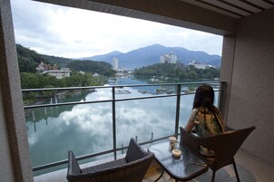 Uma varanda com cadeiras de vime e uma mesa, com vista para um rio e barcos, com edifícios ao fundo.
