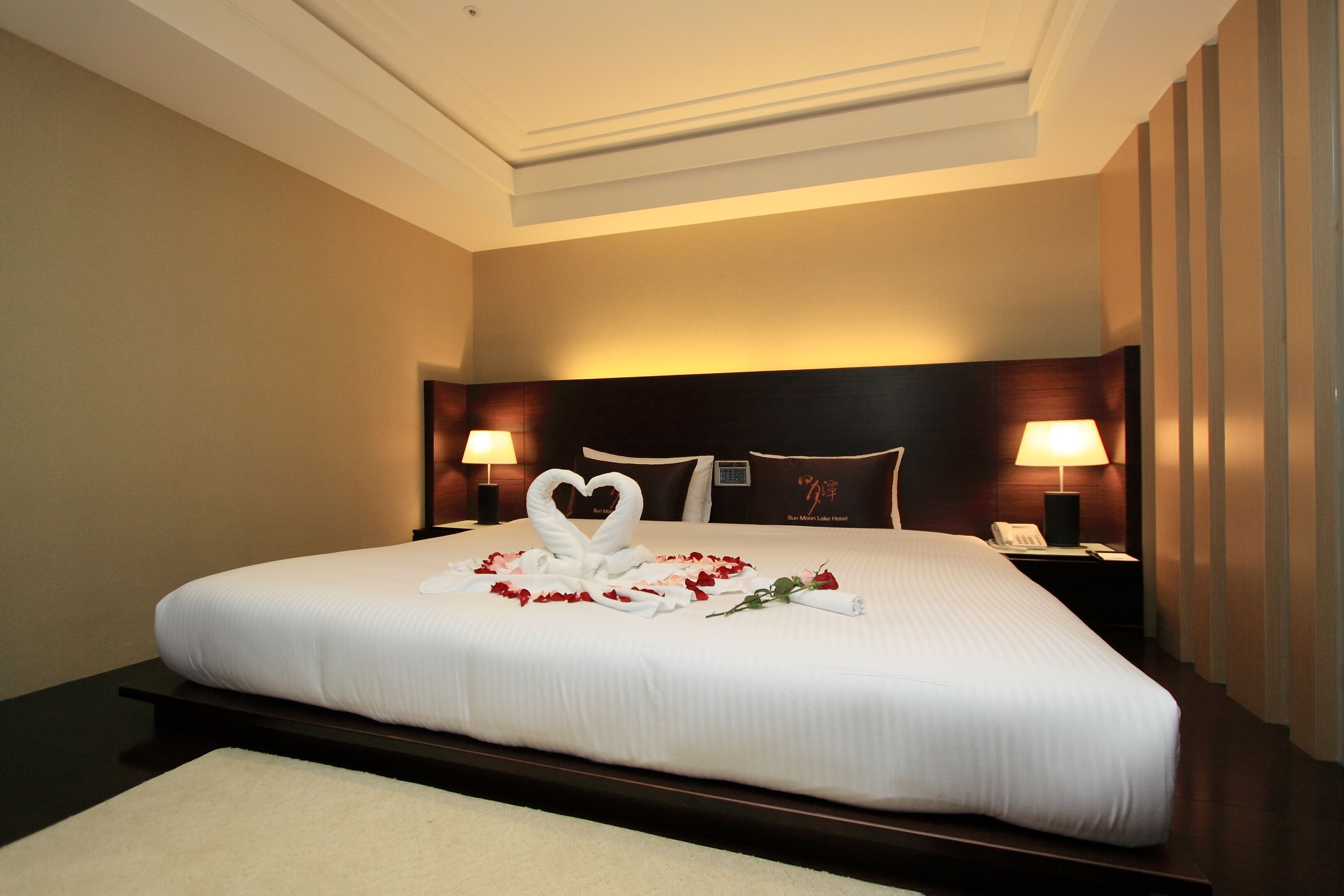 Quarto de hotel com uma cama grande, duas luminárias de cabeceira, uma cabeceira e uma mesinha de cabeceira com telefone.