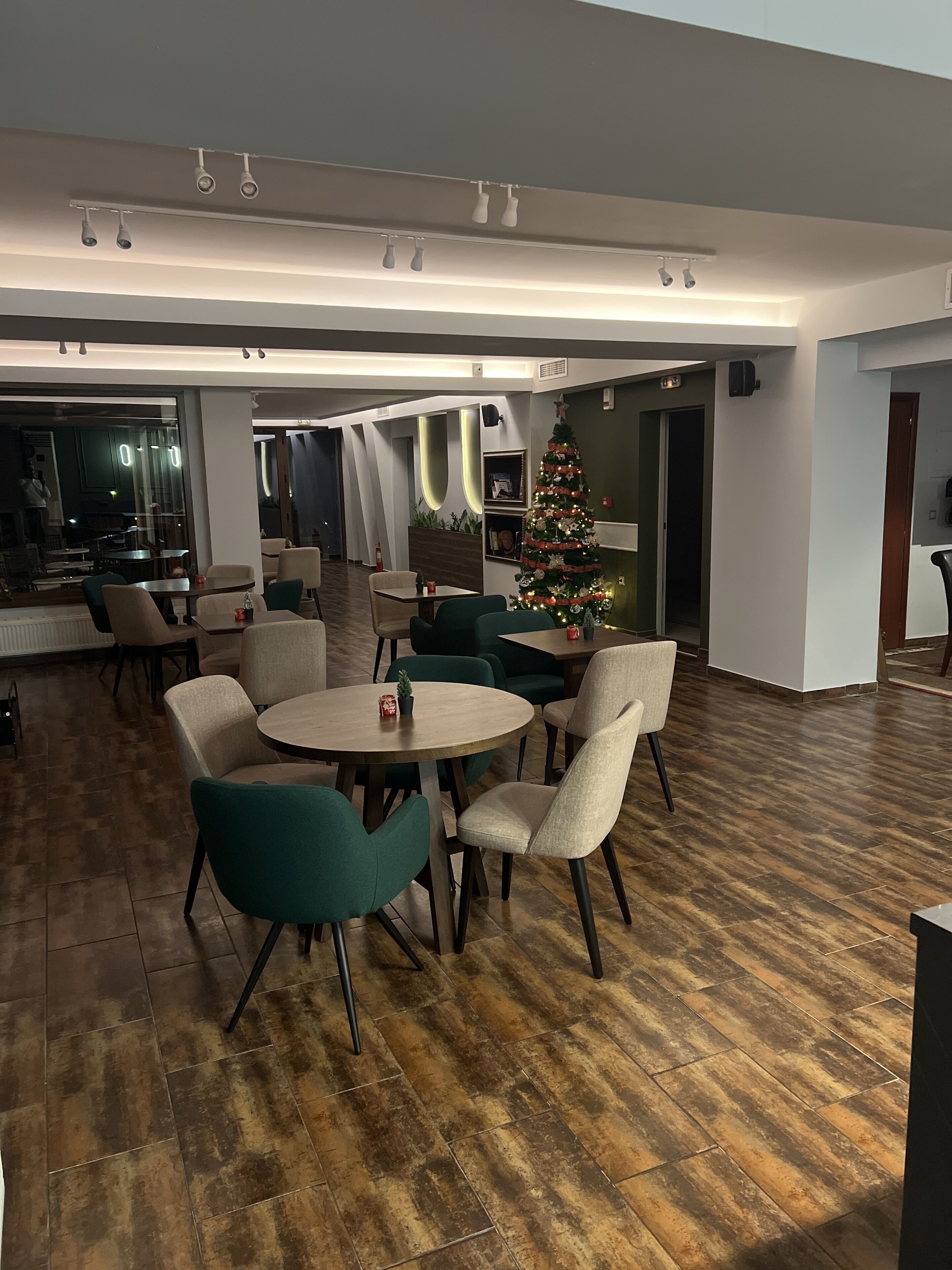 Uma área de jantar moderna com mesas e cadeiras redondas, piso de madeira e uma árvore de Natal decorada.