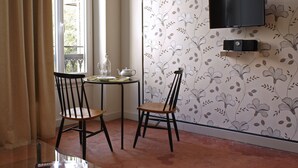 Uma área de refeições com duas cadeiras, uma mesa, uma televisão presa à parede e uma janela com cortinas.