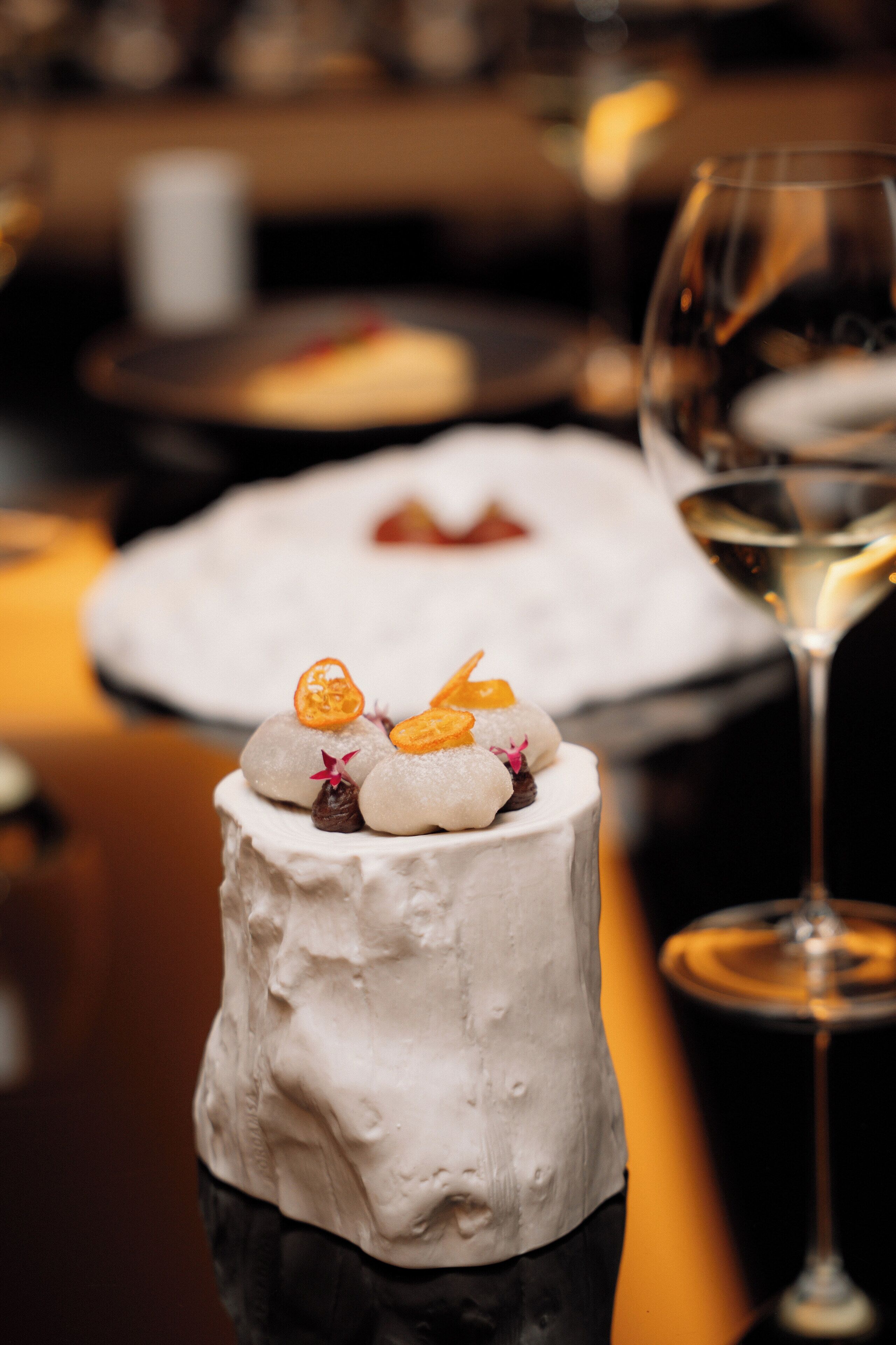 Sobremesa com superfície branca e texturizada, adornada com detalhes decorativos, acompanhada de um copo de vinho branco.
