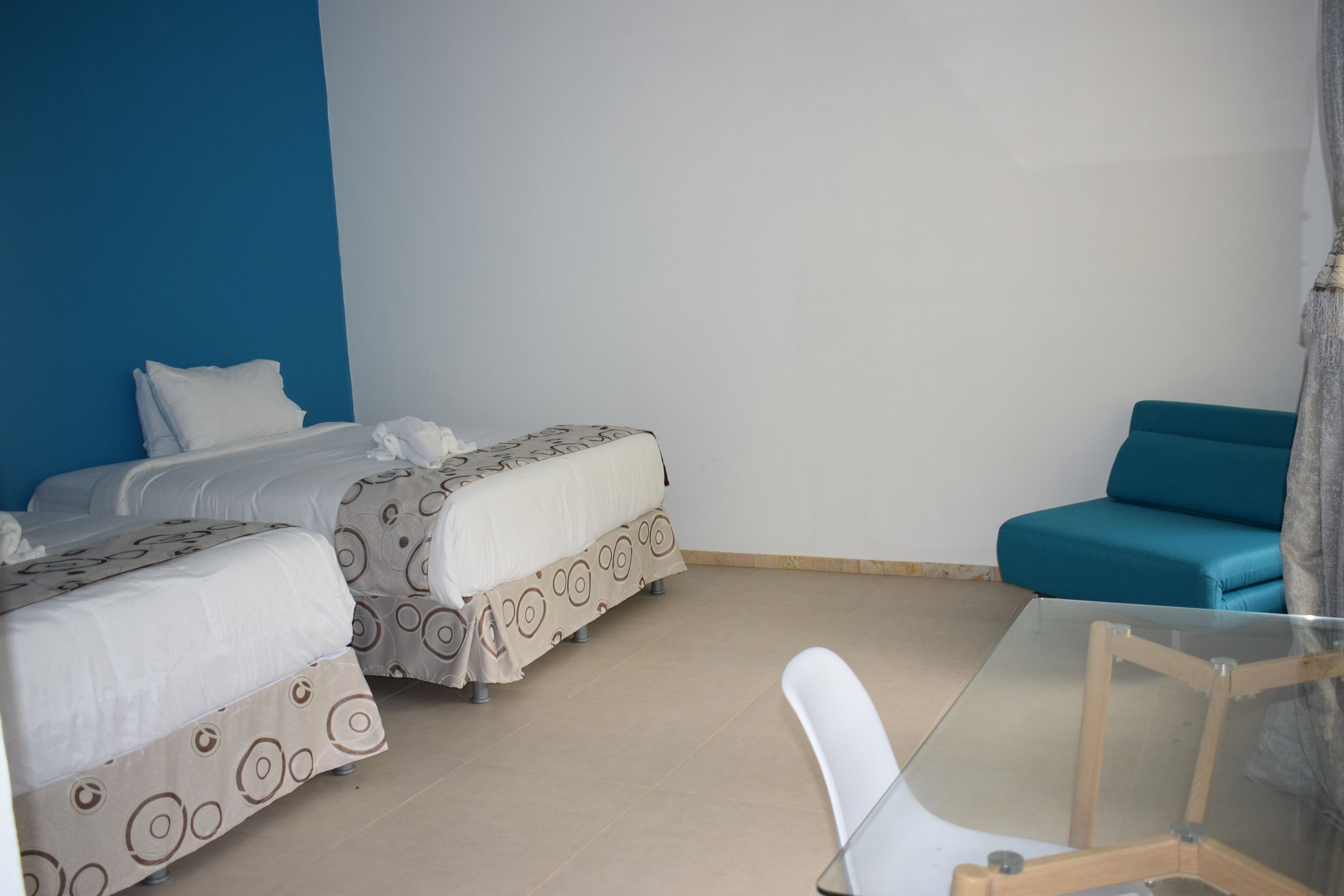 Quarto com duas camas, uma mesa de vidro e uma cadeira azul.