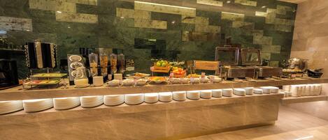 Uma área de buffet com balcão de mármore, diversos pratos e uma parede decorativa.