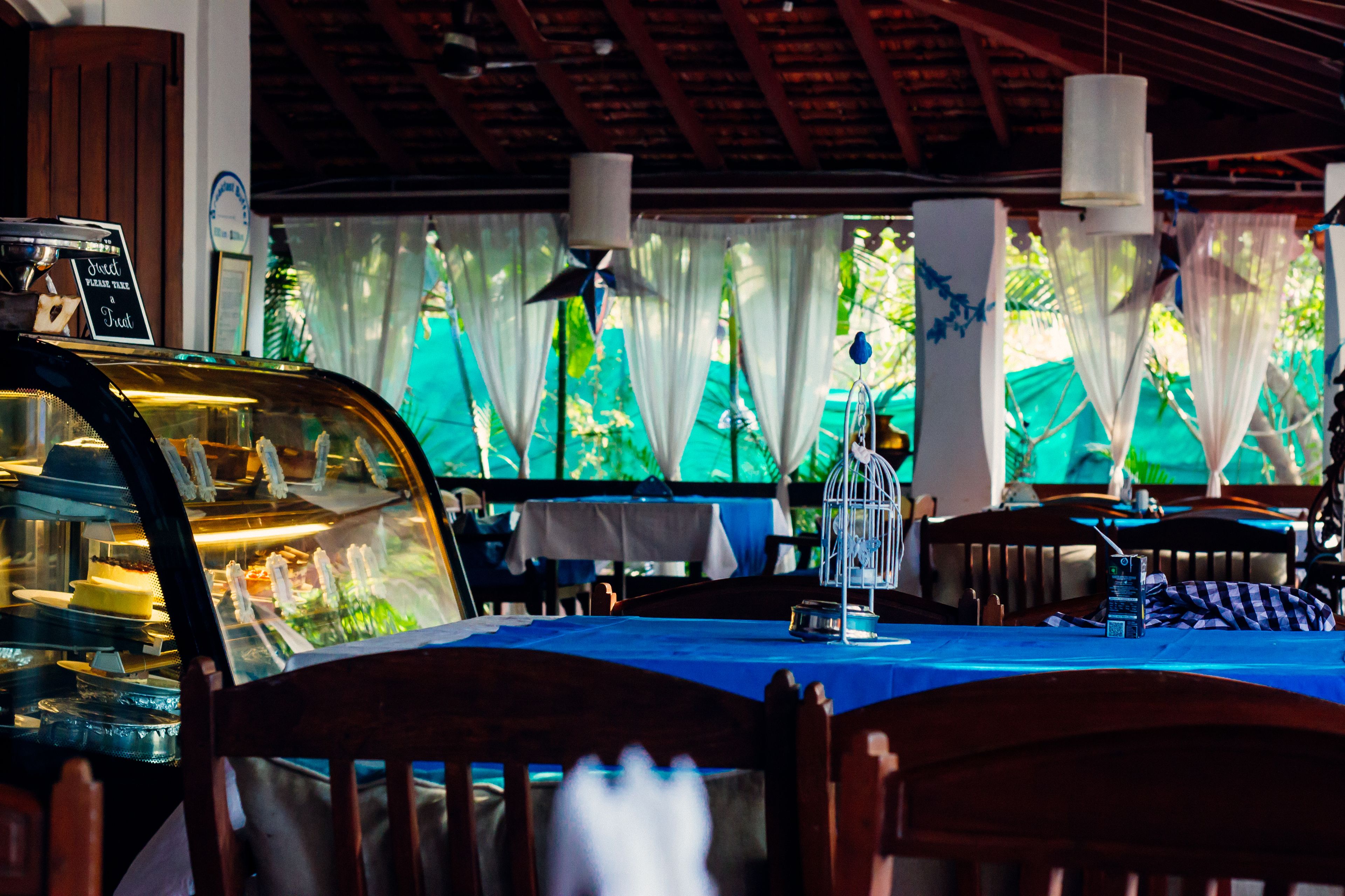 Um restaurante com toalha de mesa azul, cadeiras de madeira e uma vitrine de vidro.