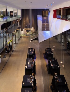 Um hall de hotel moderno com uma escadaria central, áreas de estar e um balcão de recepção.
